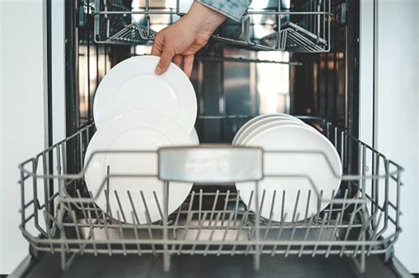 식기 세척기를 식기로 접시에 담거나 비우거나 내리는 여성 손 주방용품 라이프스타일 전망 여자는 접시를 식기 세척기에 넣거나 꺼냅니다 주부는 집안일을한다 가득 찬에 대한 스톡