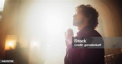 젊은 그리스도인 남자는 장엄한 교회에 경건하게 앉아 있으며 두 손을 접고 기도하는 동안 믿음과 영성의 인도를 구합니다 권력과 하나님의 사랑에 대한 종교적 믿음 측면 View