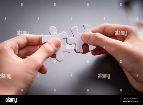 Hands Fitting Two Puzzle Pieces Together On A Gray Background Symbolizing Teamwork Connection