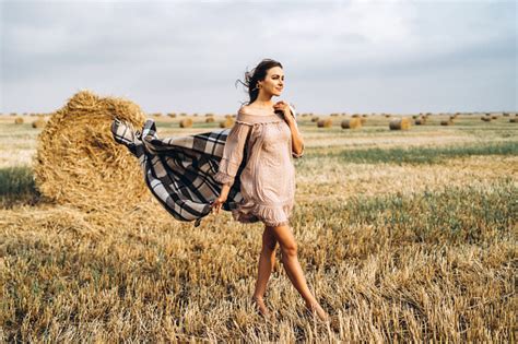 드레스와 따뜻한 격자 무늬와 아름다운 갈색 머리의 전체 길이 초상화 건초 베일과 밀 밭에서 산책을 즐기는 여자 갈색 머리에 대한