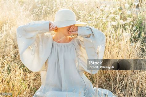 가볍고 바람이 잘 통하는 드레스와 밀짚모자를 쓴 부드럽고 알아볼 수 없는 여성이 풀잎을 들고 높은 풀밭에서 일몰의 순간을 즐기고