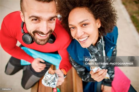 젊은 활동적인 여자는 도시 공원에 벤치에 앉아 있는 동안 그녀의 파트너와 단백질 바를 먹고 2명에 대한 스톡 사진 및 기타 이미지 2명 건강한 생활방식 건강한 식생활