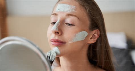 백반증 장애를 가진 매력적인 여성이 거울 앞에 앉아 팔에 거울을 들고 조심스럽게 마스크를 바르고 있는 모습의 초상화 모습 사진