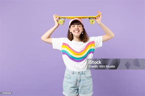 생생한 옷에 밝은 십 대 소녀 눈을 유지 하는 머리에 노란색 스케이트 보드를 들고 스튜디오에서 보라색 파스텔 배경에 고립 사람들은 진심으로 감정 라이프 스타일 개념입니다