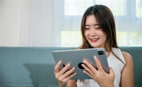 Happy Asian Woman Playing Smart Tablet At Home While Relaxing On Sofa Living Stock Image Image
