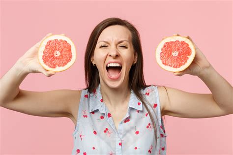 여름 옷에 미친 젊은 여자 비명 스튜디오에서 분홍색 파스텔 벽 배경에 고립 된 신선한 익은 자 몽의 Halfs를 개최 합니다 사람들은 생생한 라이프 스타일 휴식 휴가