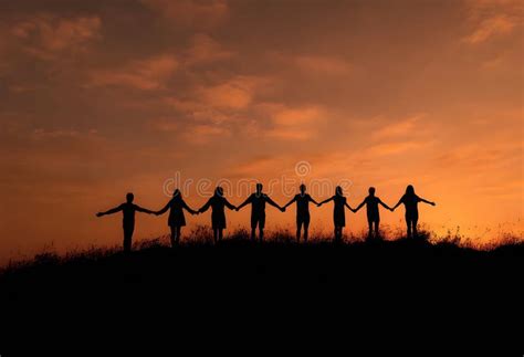 Silhouettes Of People Holding Hands At Sunset Symbolizing Unity And
