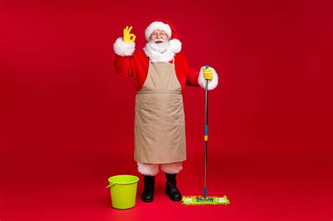 산타 클로스 회색 수염 홀드 걸레 쇼 Okey 착용 X마스 의상 앞치마 코트 모자 안경 라텍스 장갑 부츠 안경 격리 된 빨간 색 배경의 전체 길이 사진 깨끗한에 대한 스톡