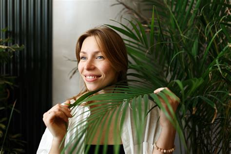 매끄럽게 그을린 피부를 가진 아름다운 젊은 여성은 이국적인 식물과 꽃을 배경으로 서서 기분 좋게 웃는다 천연 화장품 스킨 케어 건강한 생활방식에 대한 스톡 사진 및 기타