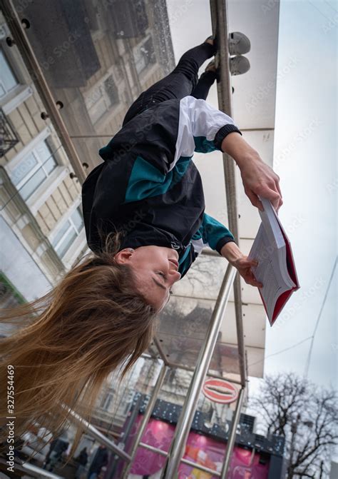Girl Hanging By Feet Upside Down In The Street And Reading Book