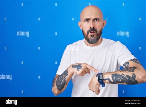 Hispanic Man With Tattoos Standing Over Blue Background In Hurry