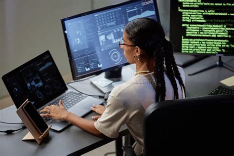 Female Programmer Coding On Laptop At Professional Workstation With Computers In Office Stock
