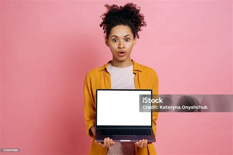 충격을 받은 아프리카계 미국인 곱슬머리 젊은 여성 카메라에 놀란 모습 빈 흰색 모형 스크린이 있는 노트북을 손에 쥐고 고립된 오렌지색 배경에 서 있다 모형 장치 화면에 대한