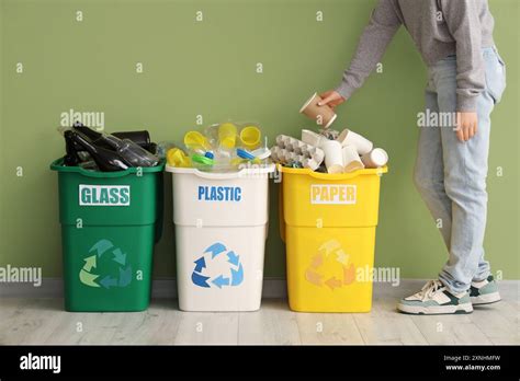Woman Putting Garbage Into Full Trash Bins With Different Types Of Waste Near Green Wall