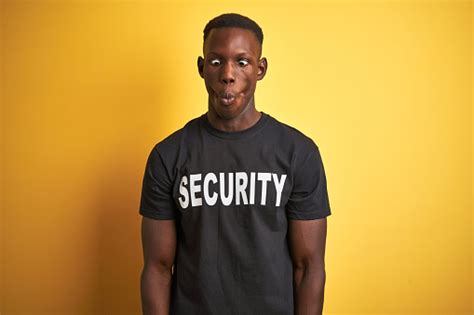 고립 된 노란색 배경 위에 보안 유니폼을 입고 아프리카 계 미국인 보호 남자는 입술 미친 코믹 한 제스처와 물고기 얼굴을 만들기 재미있는 표현 감시에 대한 스톡 사진 및