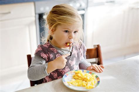 점심에 건강한 튀긴 감자를 먹는 사랑스러운 유아 소녀 집 보육 또는 보육의 부엌에 앉아 화려한 옷에 귀여운 행복 아기 아이 아이는 야채를 먹는다 먹기에 대한 스톡 사진 및