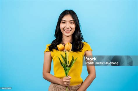 초상화 몸에 꼭 맞는 셔츠를 입은 아시아 소녀 긴 머리 꽃다발 노란색 튤립을 들고 서 있는 사람 이 꽃다발 꽃을 누군가에게 주고 싶어하는 것처럼 행복하게 미소를 지으며