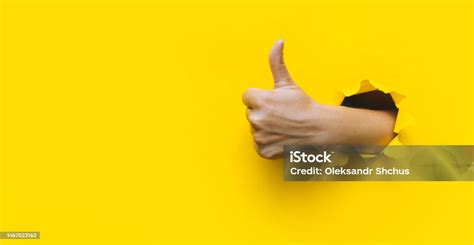 왼쪽 여성 손은 엄지 손가락 제스처 를 보여줍니다 노란 종이에 찢어진 구멍 긍정적 인 태도 승인 및 칭찬의 개념 공간을 복사합니다 구멍에 대한 스톡 사진 및 기타 이미지