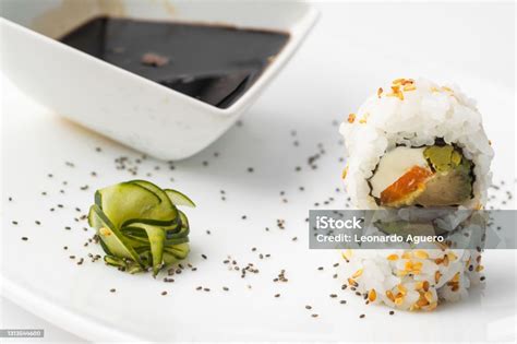 참깨와 흰 배경이 있는 흰색 접시에 오이 꽃과 간장을 곁들인 맛있는 우라마키 쌀 양귀비 씨앗 필라델피아 연어 치즈와 아보카도우라마키 레스토랑 메뉴의 정면 사진 사진 수평 0