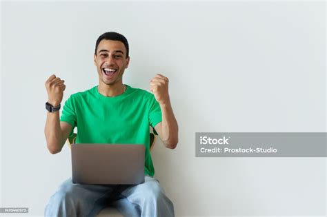 Yes 제스처를 취하고 노트북으로 의자에 앉아 흰 벽 너머로 성공 또는 성취를 축하하는 기뻐하는 아랍 남자 20 24세에 대한 스톡 사진 및 기타 이미지 Istock