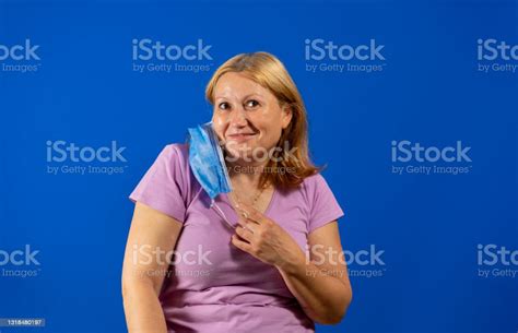 파란색 스튜디오 배경에서 고립 된 코로나 바이러스로부터 자신을 보호하기 위해 외과 용 마스크로 미소짓고 있는 보라색 티셔츠를