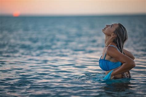 파란 수영복을 입은 소녀와 투명한 물로 하구에서 일몰을 배경으로 포즈를 취하는 밝은 파레오 건강한 생활방식에 대한 스톡 사진 및