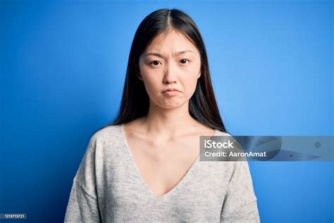 젊은 아름다운 아시아 여성은 파란색 고립 된 배경 우울위에 서 캐주얼 스웨터를 입고 분노와 두려워 울고 고민에 대한 걱정 슬픈 표정 사람 얼굴에 대한 스톡 사진 및 기타