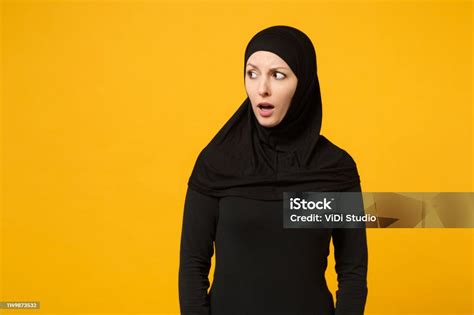 충격 무서 워 예쁜 젊은 아라비아 무슬림 여자 히 잡 블랙 옷 옆에 고립 된 노란 오렌지 벽 배경 스튜디오 초상화 사람들 종교적