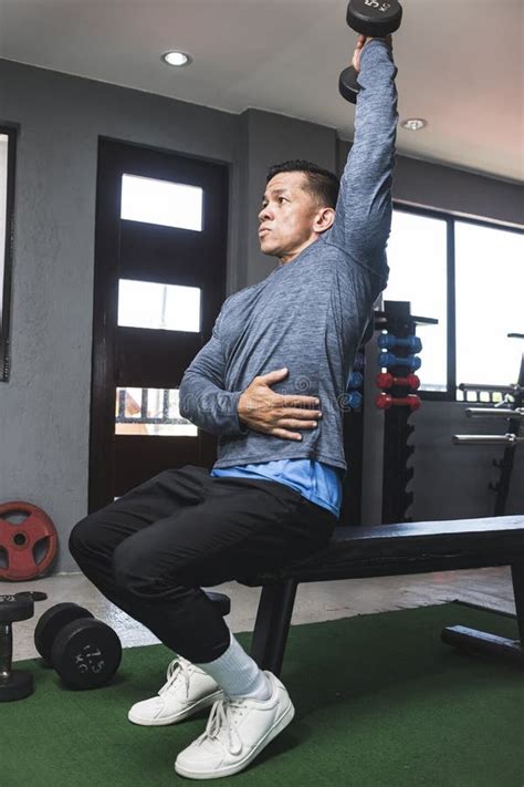 A Fit Athletic Asian Guy In A Sweatshirt Does Seated Overhead Dumbbell One Arm Tricep Extensions
