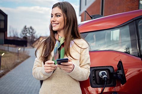 그녀의 집 앞에서 전기 자동차를 충전 하는 젊은 여자의 초상화 전기 자동차 대체 연료 자동차에 대한 스톡 사진 및 기타 이미지 전기 자동차 대체 연료 자동차 충전