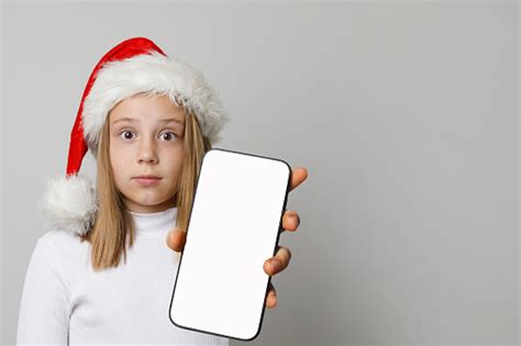 회색 배경에 빈 빈 흰색 화면 디스플레이와 함께 스마트 폰을 들고 산타 모자를 쓴 놀란 흥분 어린이 소녀 8 9 살에 대한 스톡 사진 및 기타 이미지 Istock