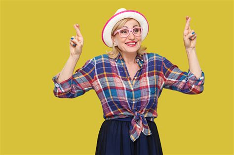 승리와 함께 희망을 기쁘게 하는 현대 세련 된 성숙한 여 자가 모자와 안경에 서 있는 캐주얼 스타일의 초상화와 교차 손가락과 보고 금발 머리에 대한 스톡 사진 및 기타