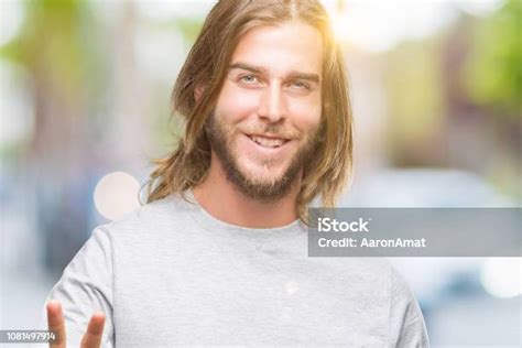 격리 된 배경에 보여주는 손가락 승리 표시를 하 고 카메라를 보고 웃 긴 머리를 가진 젊은 잘생긴 남자 번호 2입니다 긍정적인 감정 표현에 대한 스톡 사진 및 기타 이미지