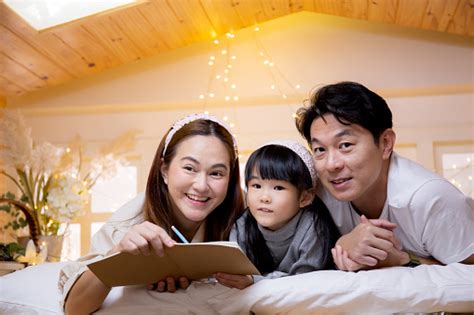 엄마와 아빠가 누워 숙제를 가르치고 집 침실에서 딸과 함께 숙제를 가르치고 엄마와 아빠가 아이와 함께 학업을 설명하고 라이프