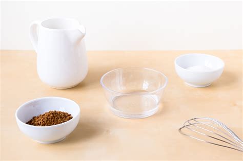 커피 달고나를 만드는 방법 단계별 사진 지시 1단계 준비 재료 인스턴트 커피 설탕 물 우유 및 나무 배경에 채찍질을위한 거품기