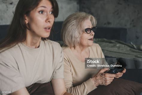 딸과 함께 있는 시니어 여성은 퇴근 후 거실 소파 근처 바닥에 앉아 손에 조이스틱을 들고 즐거운 시간을 보내고 있다 가족 활동 개념의 세대 차이 선택적 초점 2명에 대한