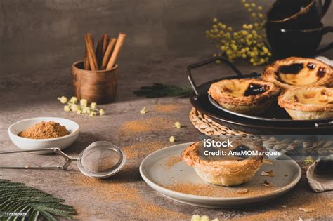 전통적인 포르투갈 페이스트리 파스텔 데 나타 또는 파스텔 드 벨렘은 소박한 보드에 전통적인 트레이에 계피 파우더를 드실 수 있습니다 달걀 타르트 가루로 빻은에 대한 스톡