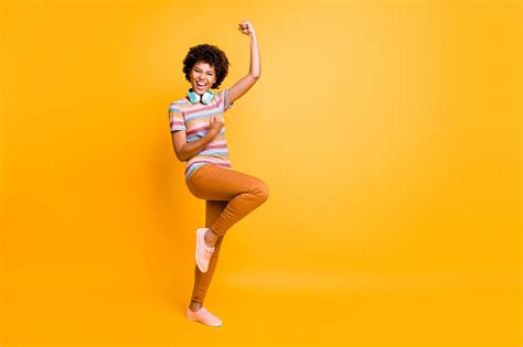 전체 길이 바디 사이즈 사진 의 쾌활 한 승리 흥분 미친 소녀 비명 예 착용 바지 바지 신발 무선 헤드폰 위에 고립 된 노란색 선명한 색상 배경 T 셔츠에 대한 스톡 사진