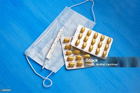 알약 온도계 파란색 배경에 의료 얼굴 마스크 상단보기 응급 처치 질병 중 관리 의학 의약품 건강 아날로그 수은 온도계 및 의료 용 마스크 옆에 노란색 캡슐 0명에 대한 스톡