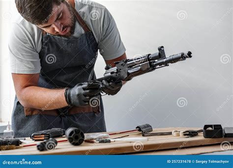Close Up Of Young Man In Apron Disassembling A Gun Above The Table