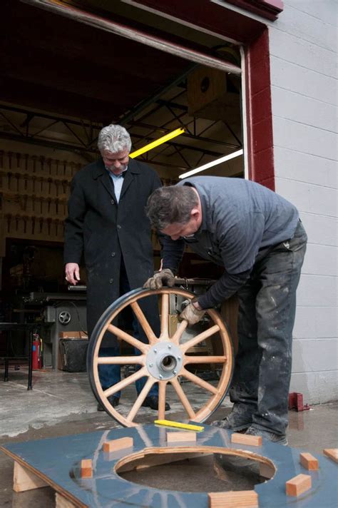 Two Men Working On A Wooden Wheel In A Garage