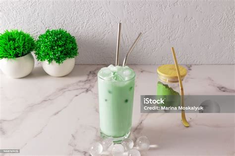 금속 짚과 둥근 얼음 조각이 있는 키가 큰 유리잔에 담긴 말차 달곤 녹차 유리 항아리에 녹차 가루 차가운 커피의 대안 기포에