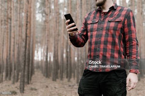 남자가 빨간색에서 격자 무늬 셔츠와 검은 바지를 군 그의 손에 스마트폰 보유 소나무 숲에서 길을 공간에 복사 합니다 격 조