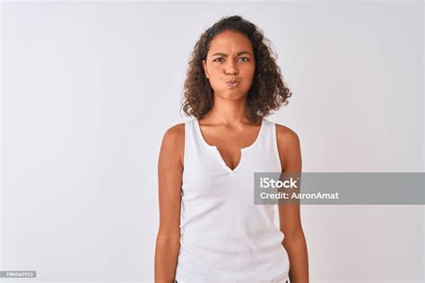 재미 있는 얼굴과 고립 된 흰색 배경 퍼핑 뺨 위에 서 캐주얼 티셔츠를 입고 젊은 브라질 여성 공기 미친 표정으로 입이 팽창