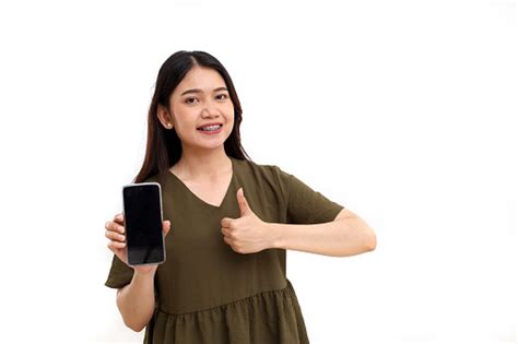 행복한 젊은 아시아 여자는 휴대폰의 빈 화면과 엄지손가락을 보여주면서 서 있다 흰색으로 격리 25 29세에 대한 스톡 사진 및