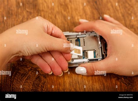 The Insertion Of The SIM Card In A Smartphone On Wooden Table Girl S Hands Insert SIM Card In