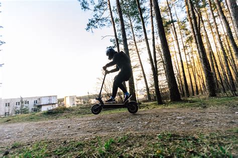 숲 밖에서 전기 푸시 스쿠터를 운전하는 남자의 남성 초상화 사람은 검은 보호 헬멧과 캐주얼 코트를 착용합니다 킥스쿠터를 타는