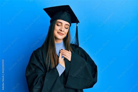 Beautiful Brunette Young Woman Wearing Graduation Cap And Ceremony Robe Smiling With Hands On