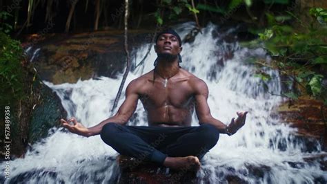 Black Young Male Model Sits In Meditative Yoga Pose In A Waterfall With