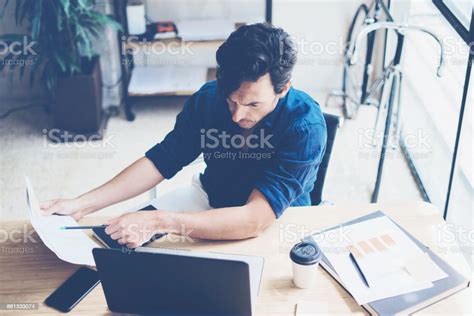 나무 테이블에 앉아 있는 동안 노트북에 밝은 직장에서 일 하는 젊은 동료 남자는 그의 손에 문서를 분석 합니다 흐리게 배경입니다 수평 Private Viewing에 대한